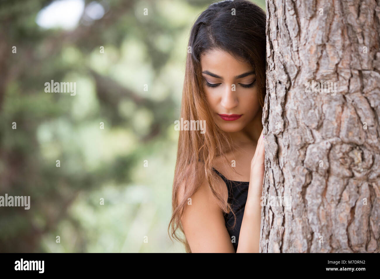 Sad young woman hiding behind a tree Stock Photo - Alamy