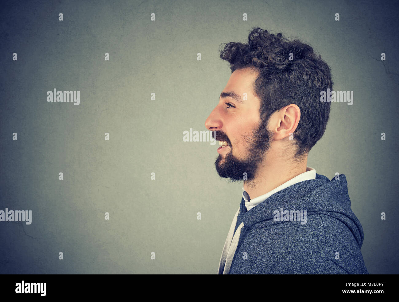 Side view of young hipster man with beard laughing and looking away on ...