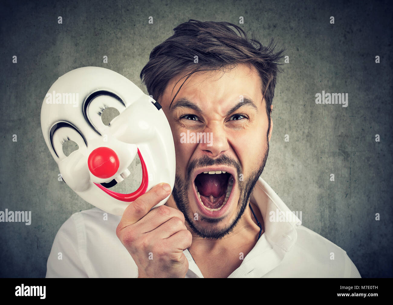 Portrait young angry screaming man taking off a clown mask isolated on ...