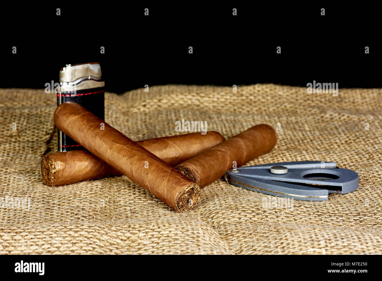 Three Cuban cigars with a cutter and a lighter on a black background ...