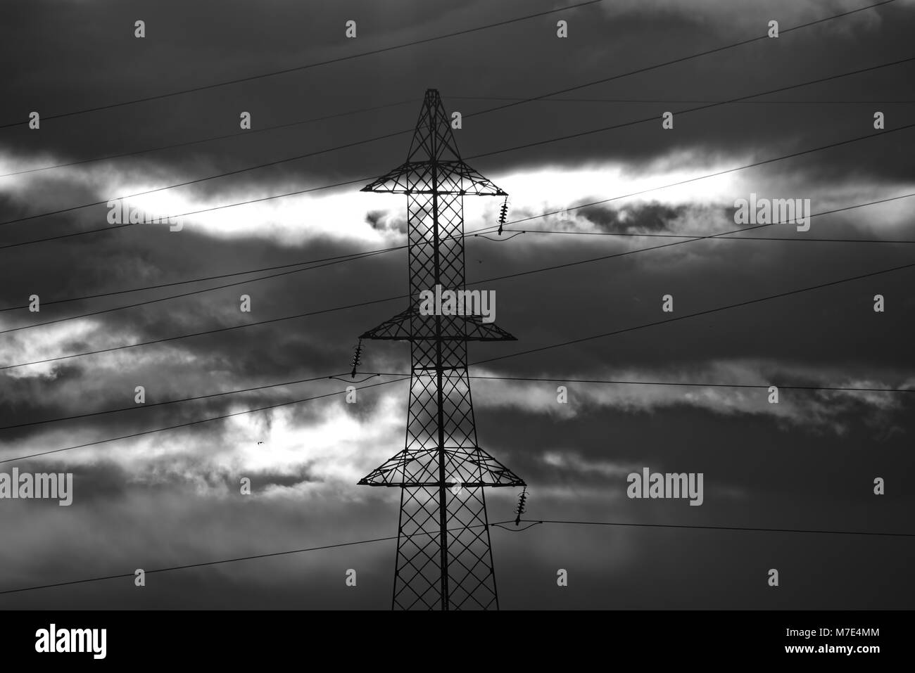 A power line pylon in silhouette, backlit by sunlight with dramatic ...