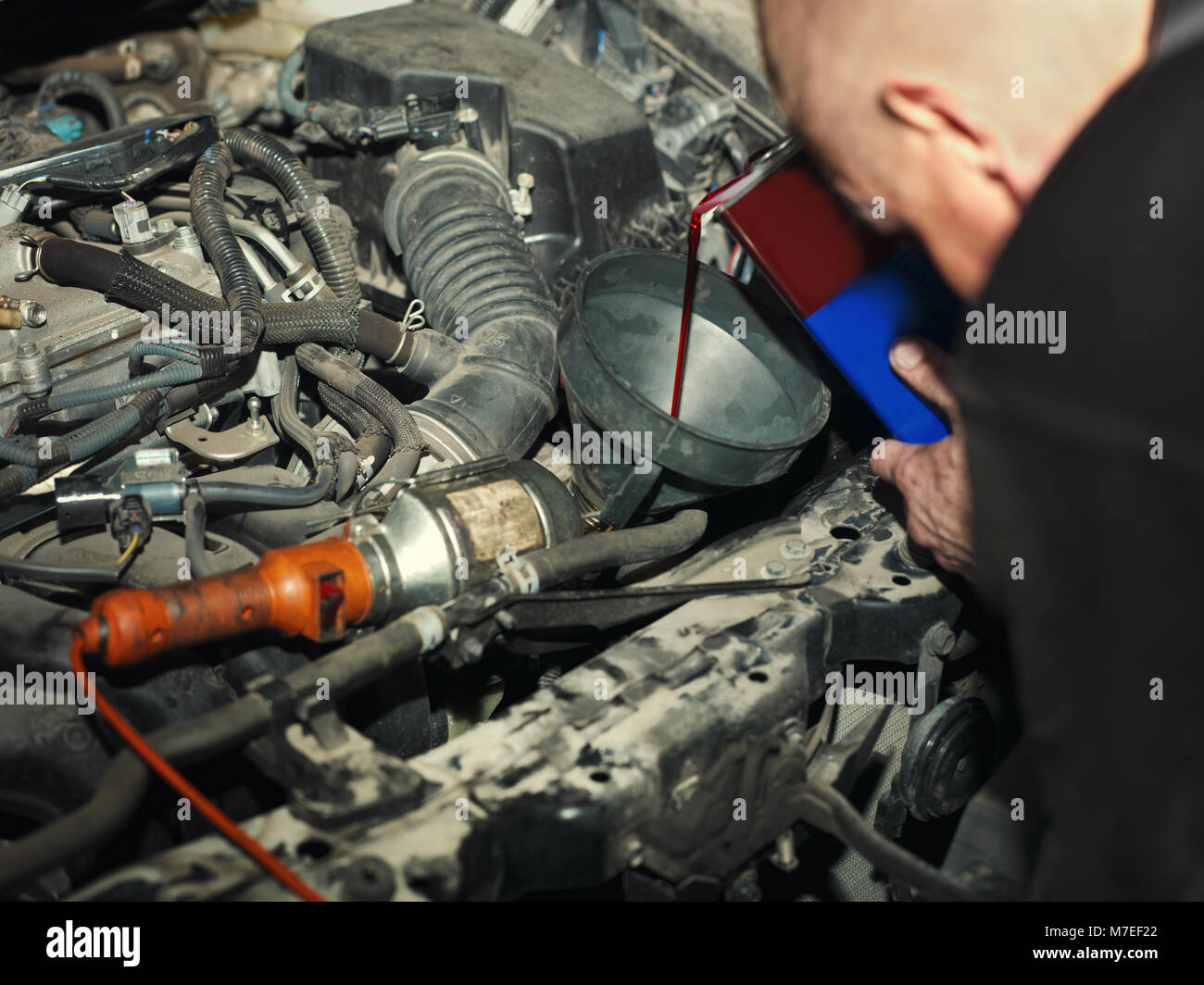 A man pouring oil into a car engine, filtered indoor closeup Stock ...