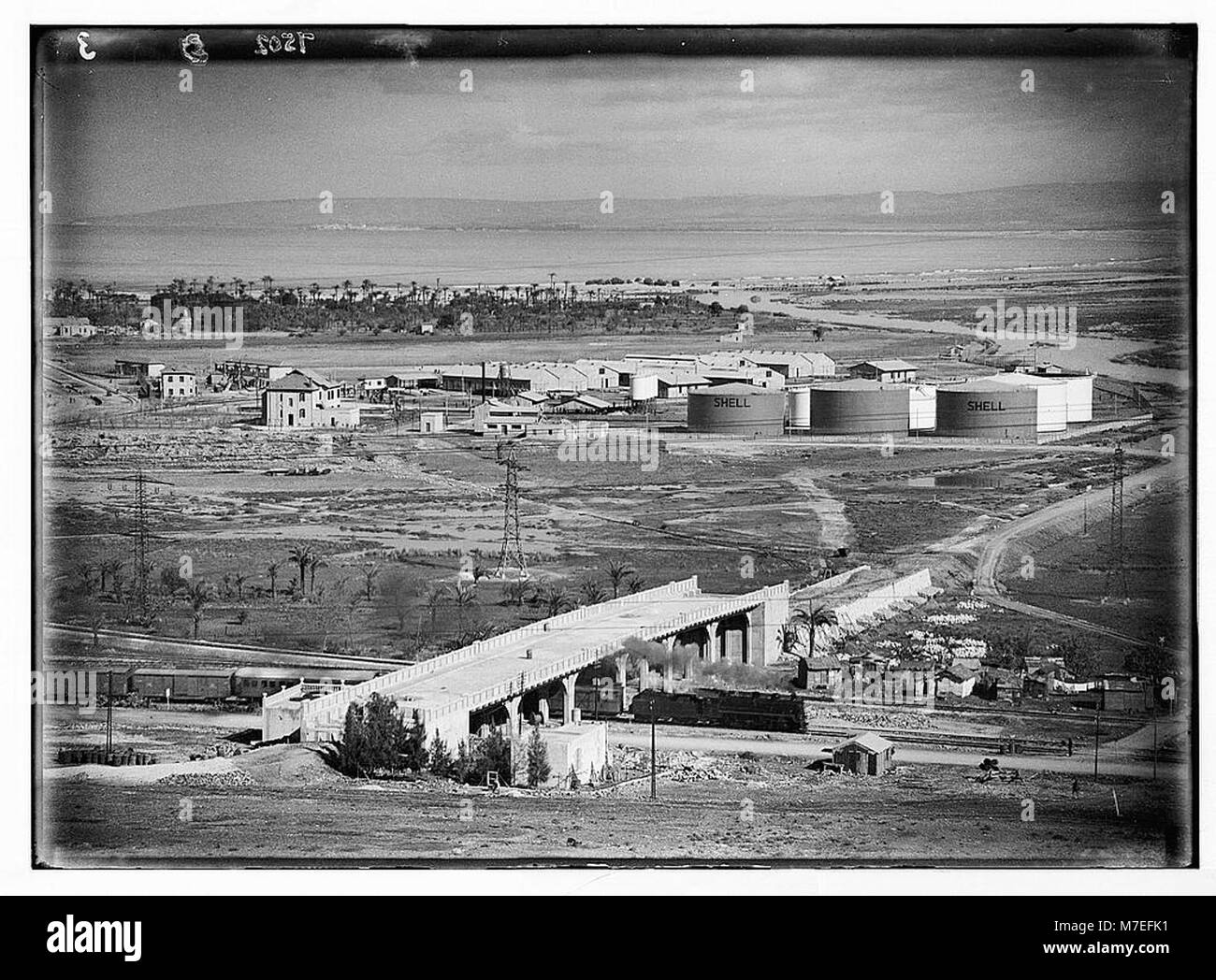 The image depicts 'Shell' oil tanks near Haifa, with a bridge spanning ...