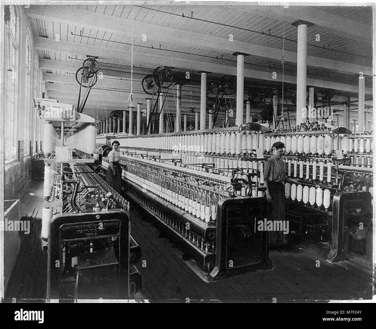 This image depicts two women working at machines in a textile factory ...