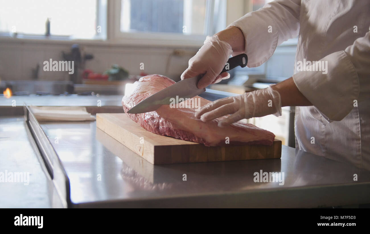 Butcher cutting large piece of fresh raw meat lying on a wooden board ...