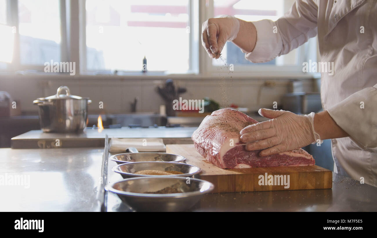 Butcher adding spices into large piece of fresh raw meat lying on a ...