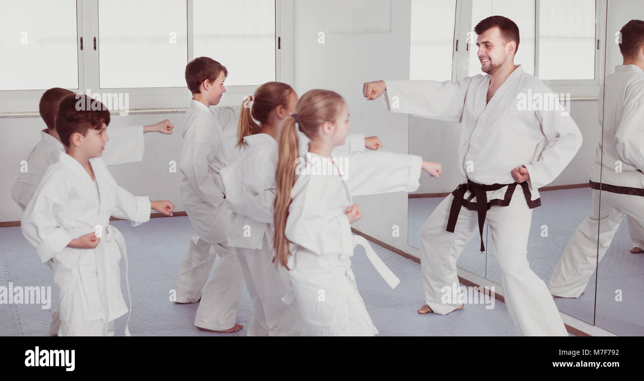 Smiling children doing karate kicks with male coach during karate class ...