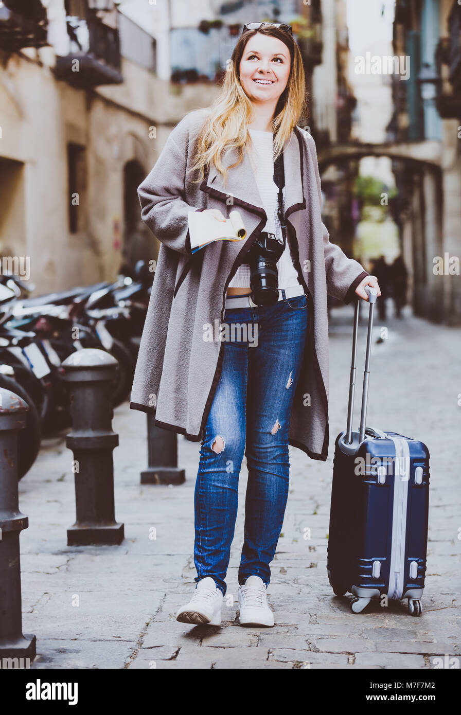 Smiling young tourist blond girl taking a walk in the town streets with ...