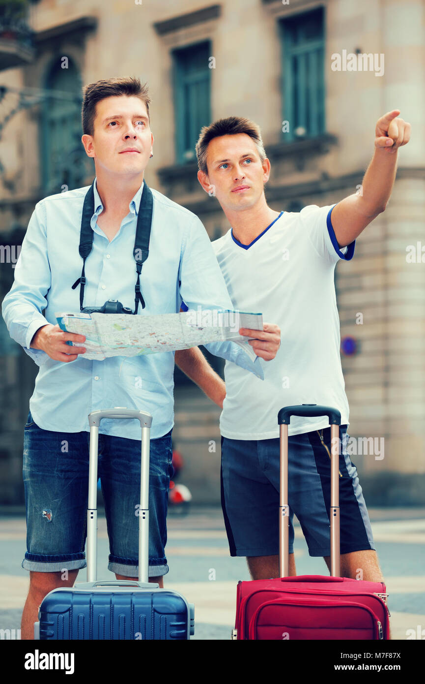 positive men having a map and looking for her route in the street of ...