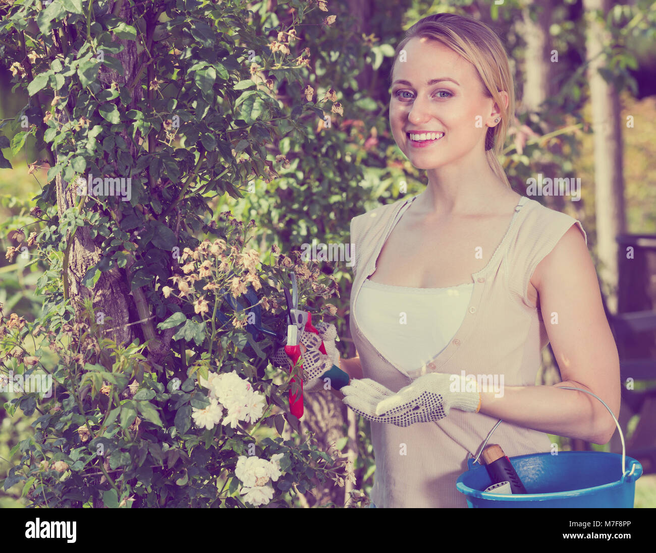 portrait of cheerful female gardener with working tools standing ...