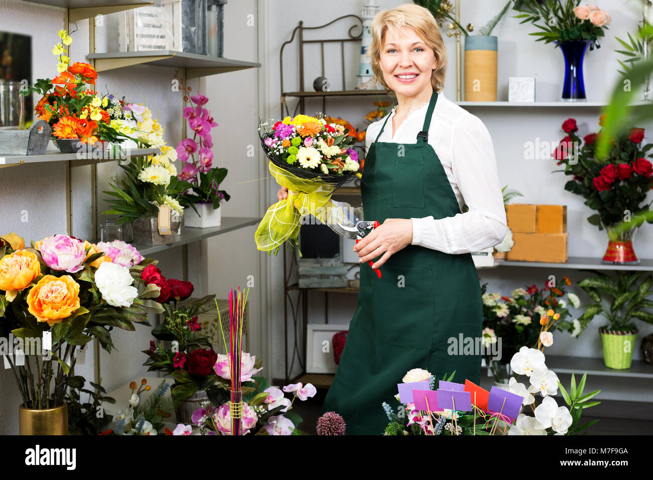 Attractive woman florist in apron holding scissors and fixing flowers ...