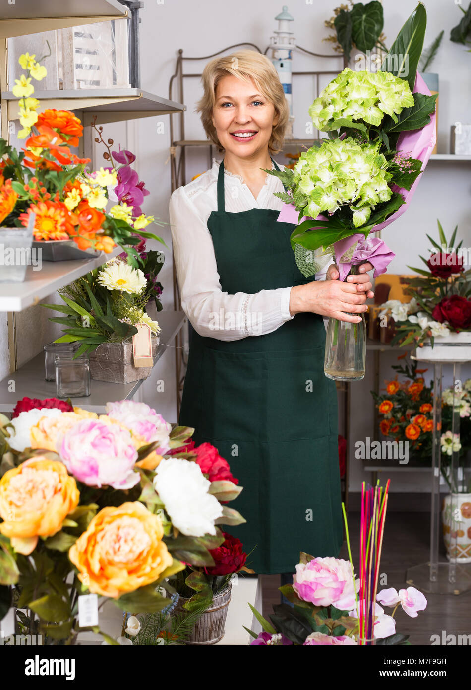 Smiling mature woman florist in apron holding bunch of flowers in ...