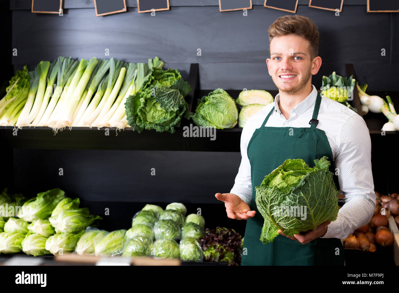 Happy male shop assistant demonstrating cabbage in grocery shop Stock ...