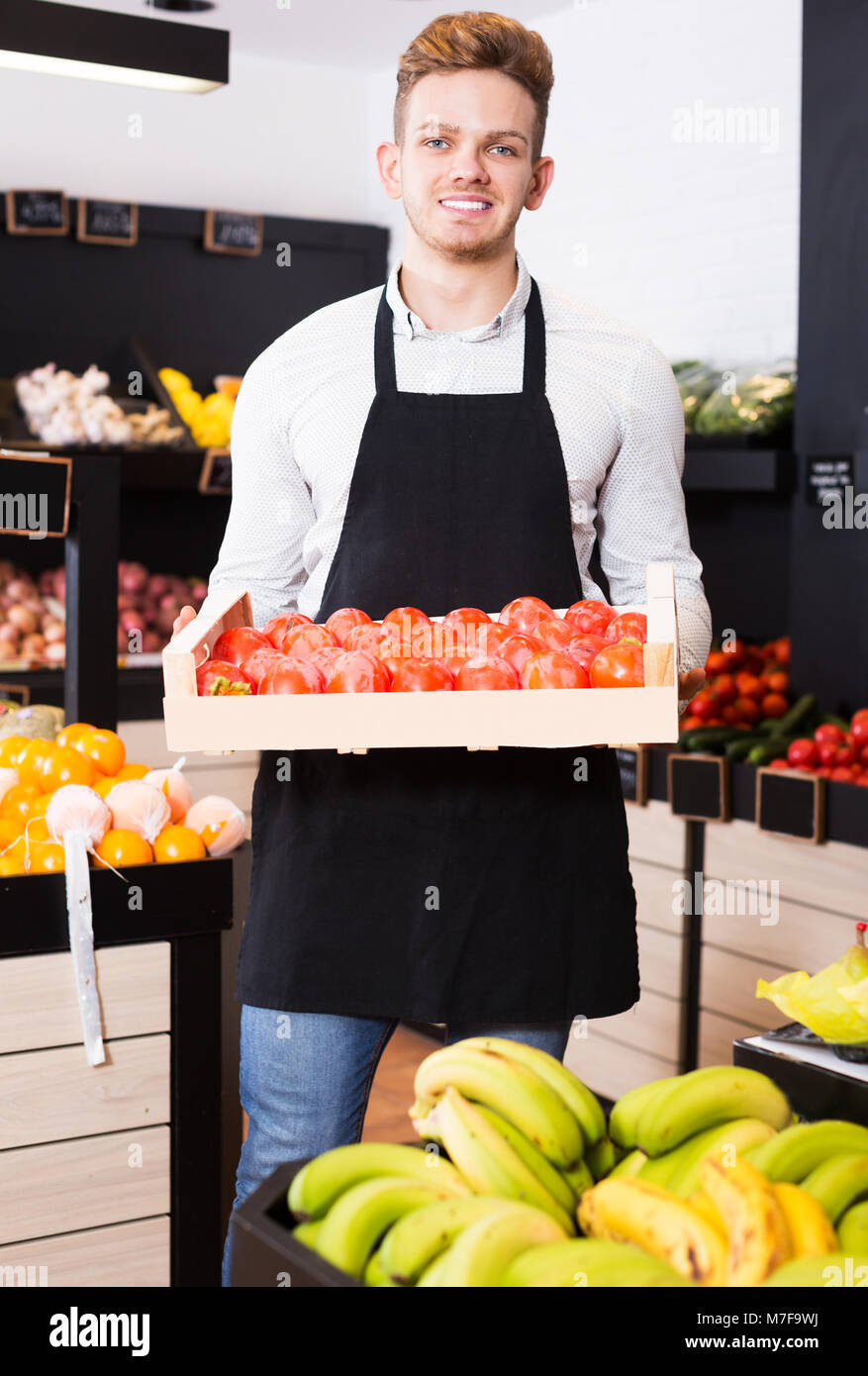 Male shop assistant transporting box of persimmons in grocery shop ...