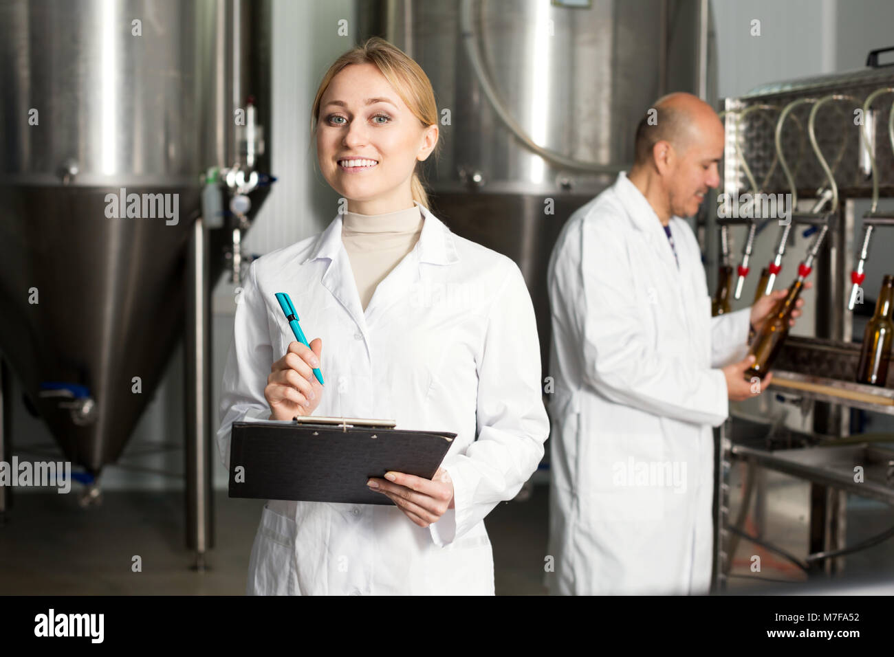Happy girl wearing uniform standing among brewery stainless equipment ...