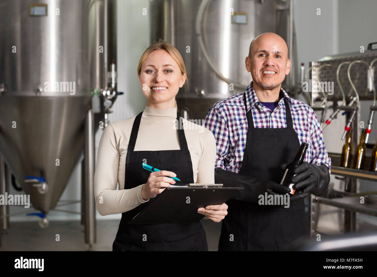 Cheerful man and woman wearing a uniform standing among a brewery ...