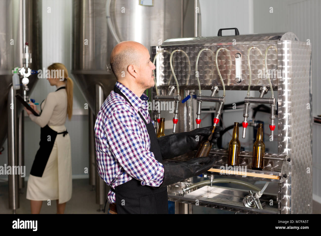 Positive man employee bottling beer in glass bottles on modern facility ...