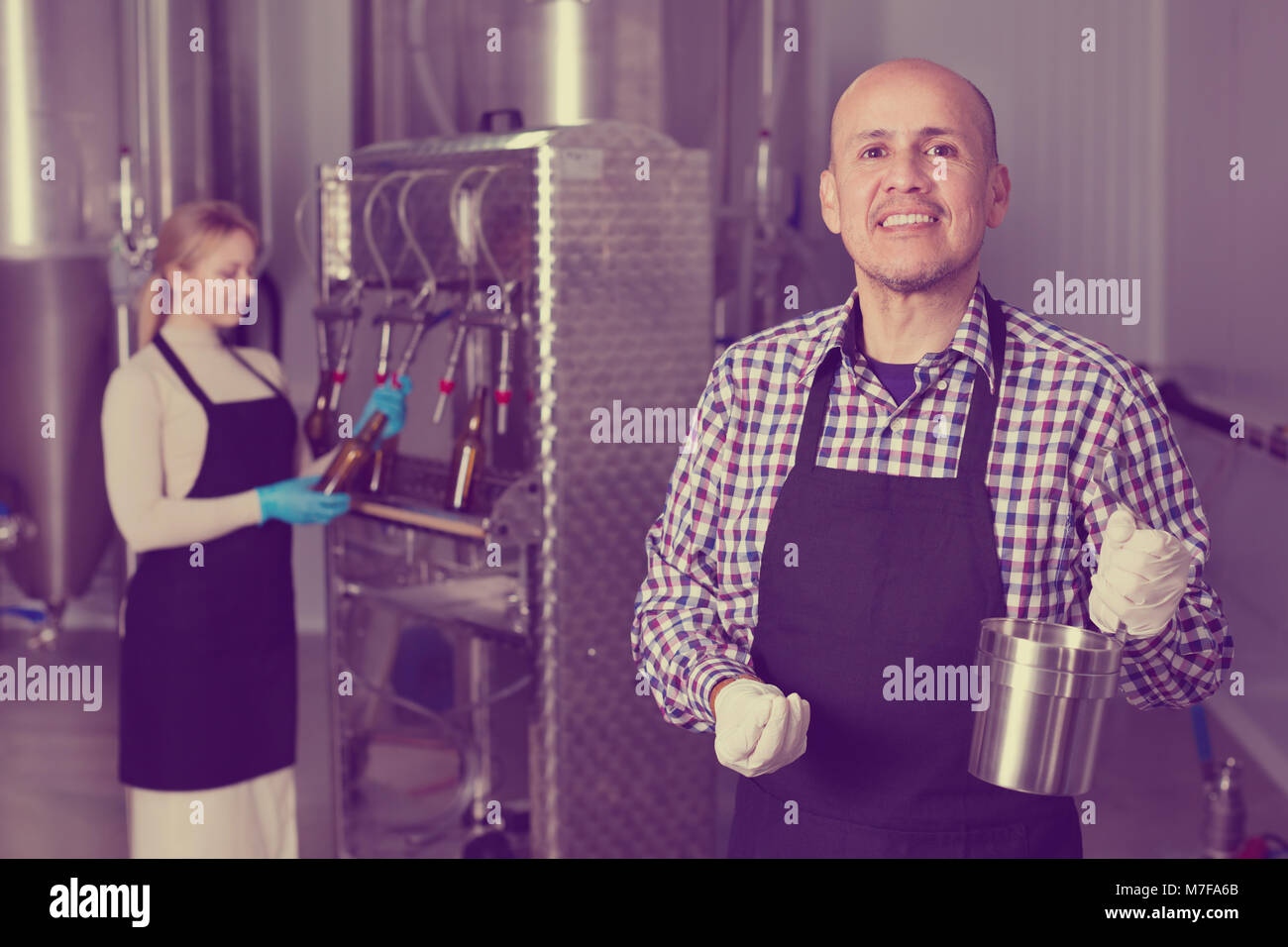 Mature cheerful man wearing the uniform standing among brewery ...