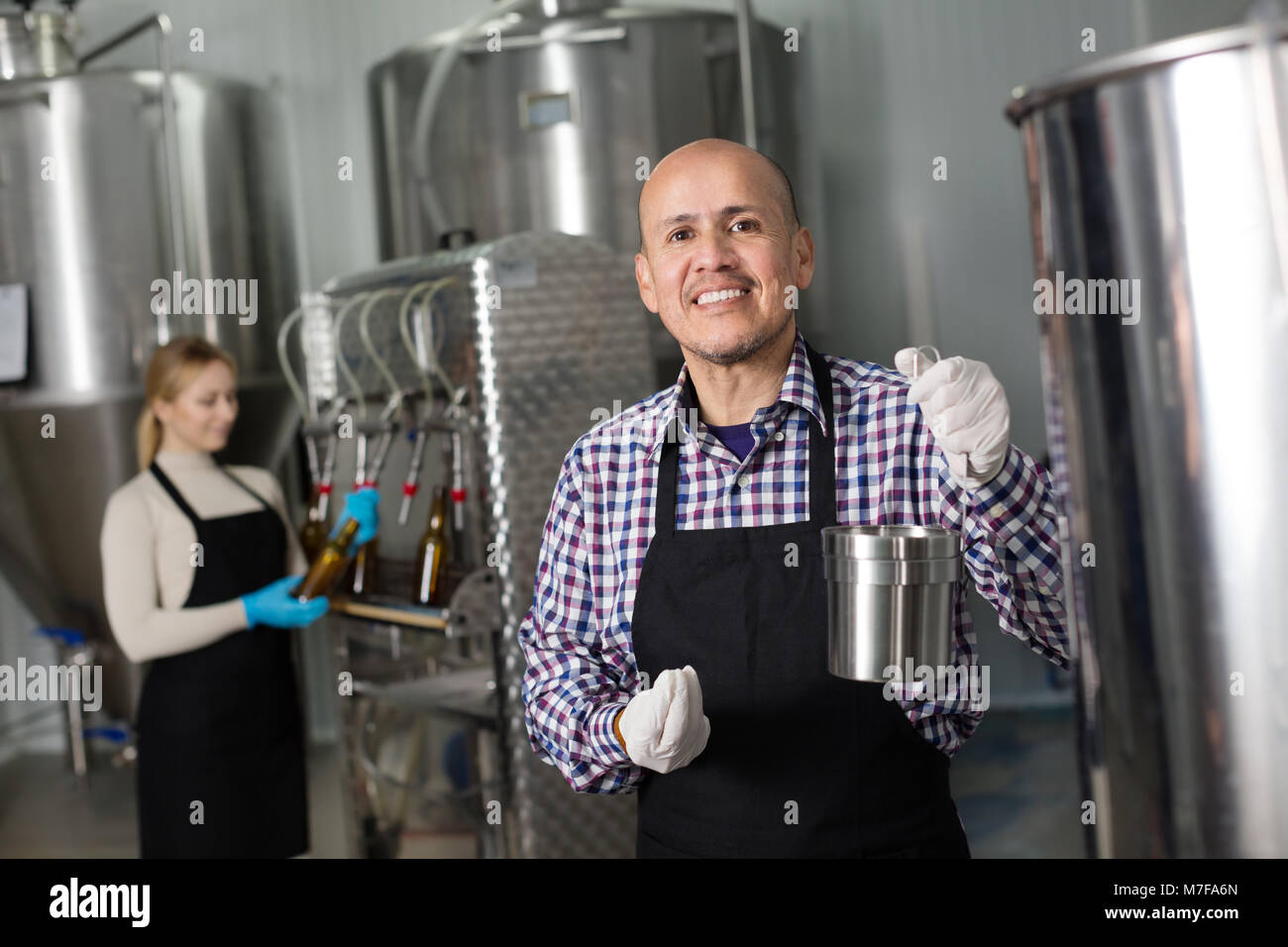 Mature cheerful man wearing the uniform standing among a brewery ...