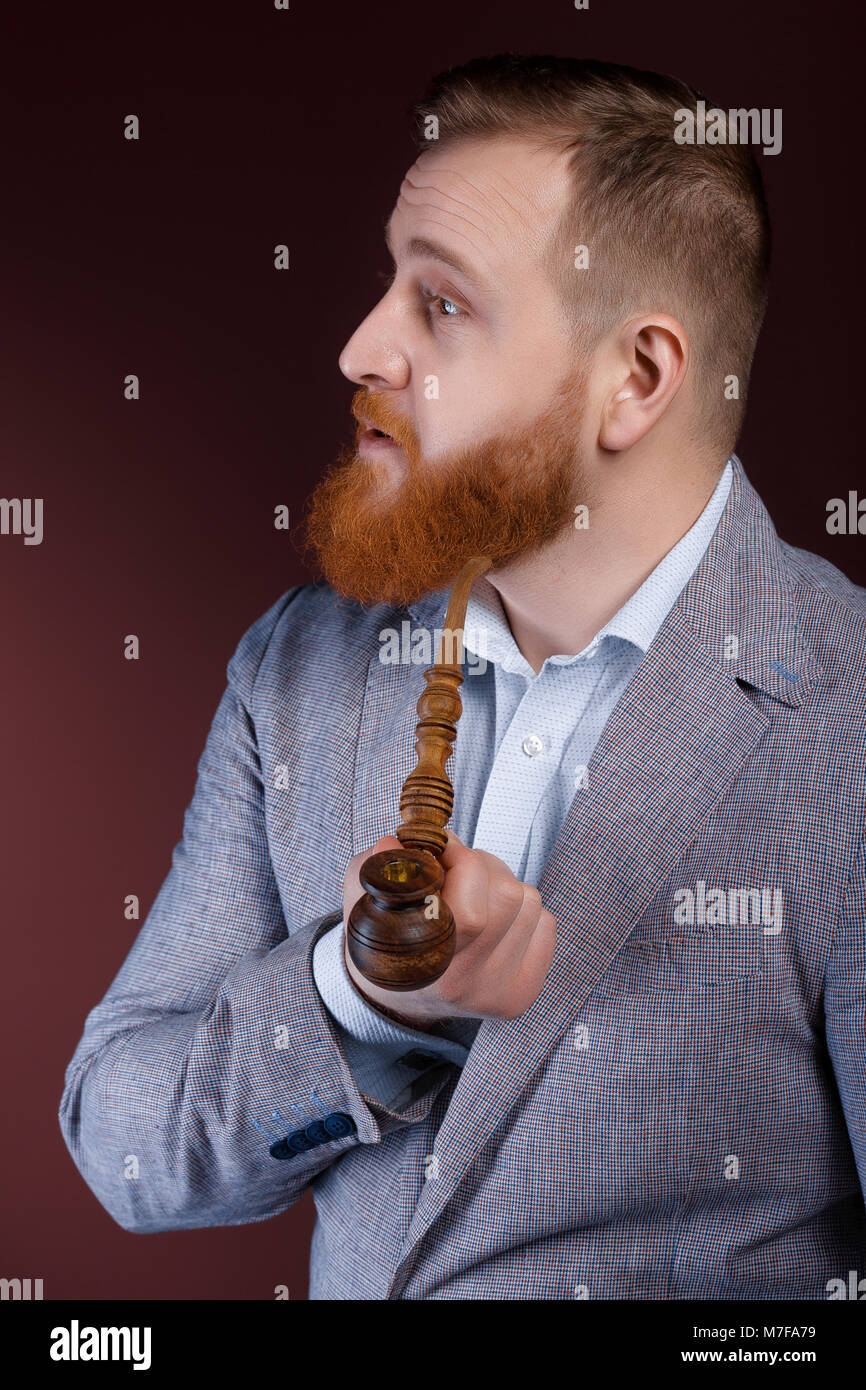 portrait of a red bearded man smoking a pipe on a brown background ...