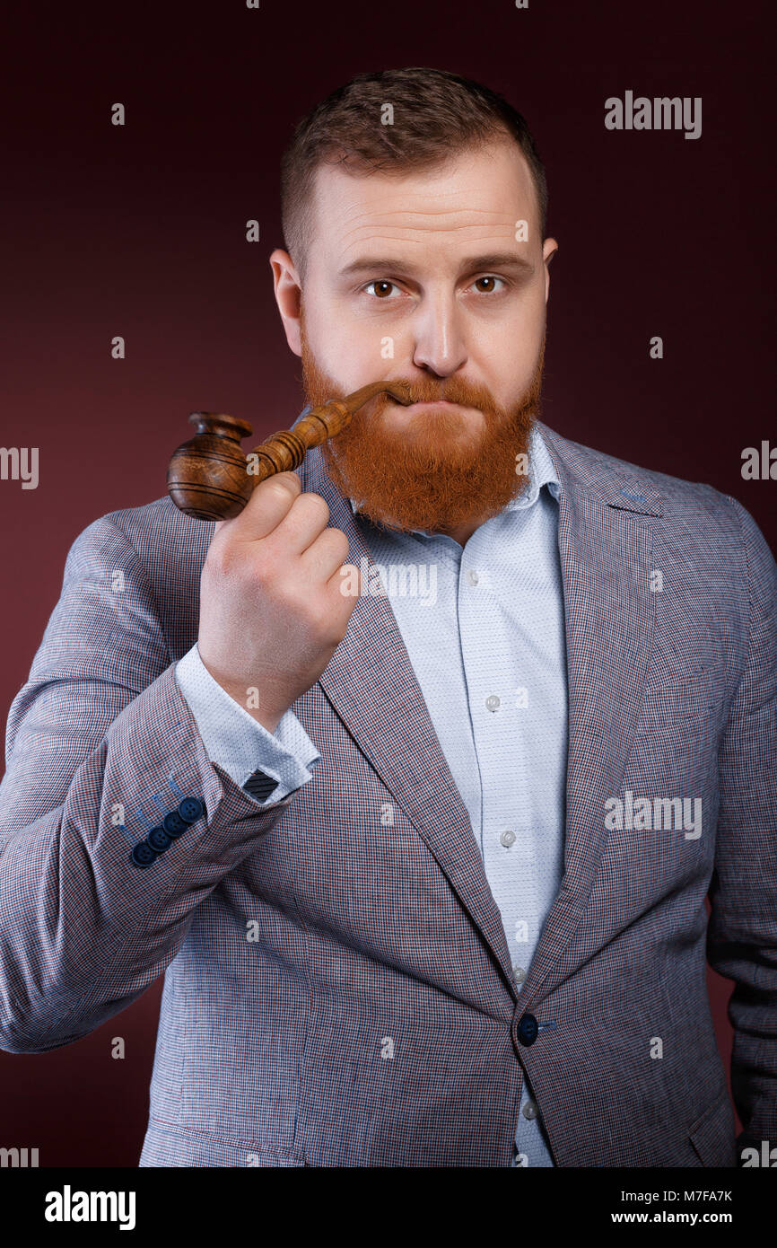 portrait of a red bearded man smoking a pipe on a brown background ...