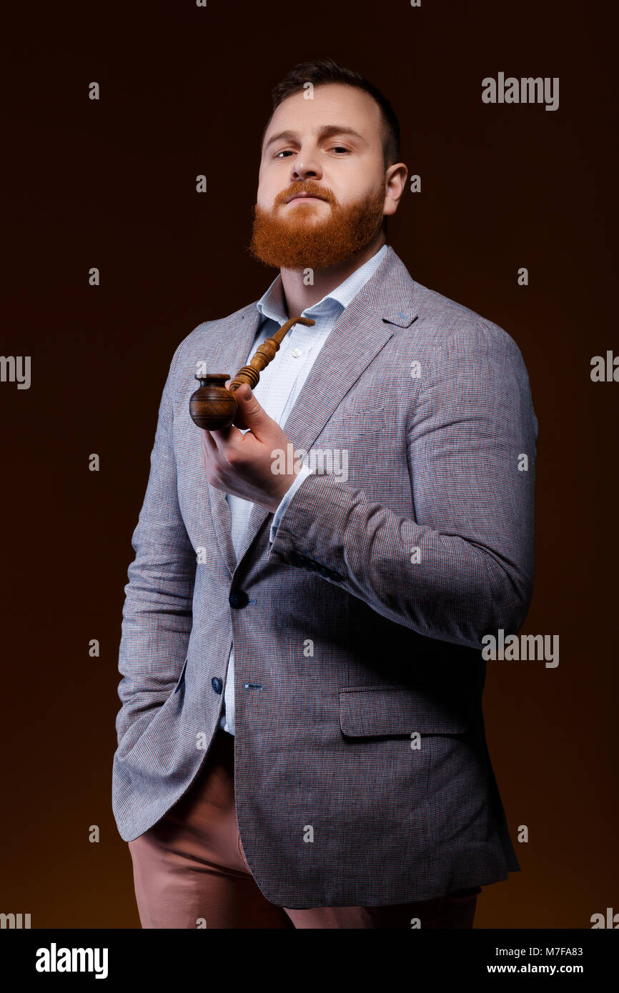 portrait of a red bearded man smoking a pipe on a brown background ...