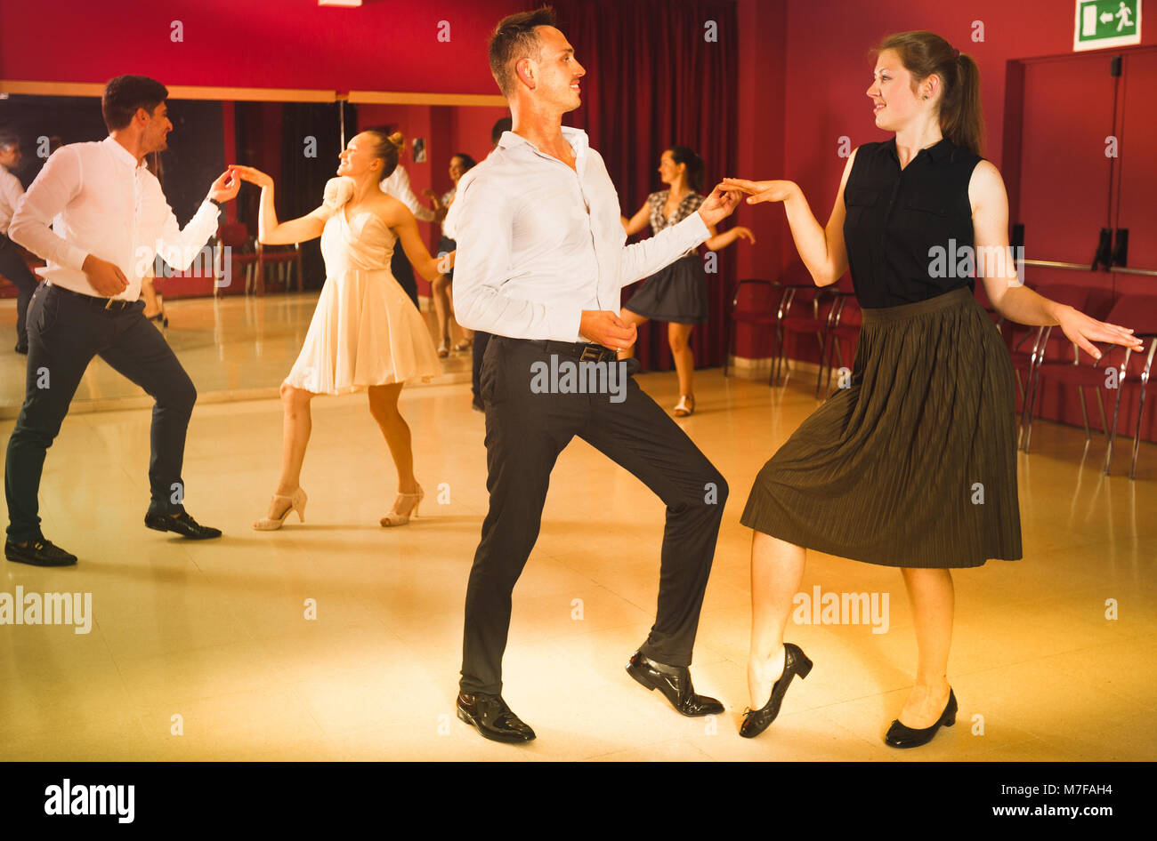 Young smiling people practicing vigorous twist movements in dance class ...