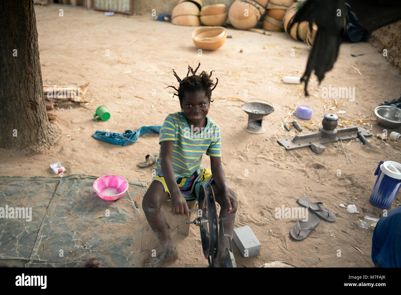 A young girl operates a wheel that drives bellows to fan the fire used ...
