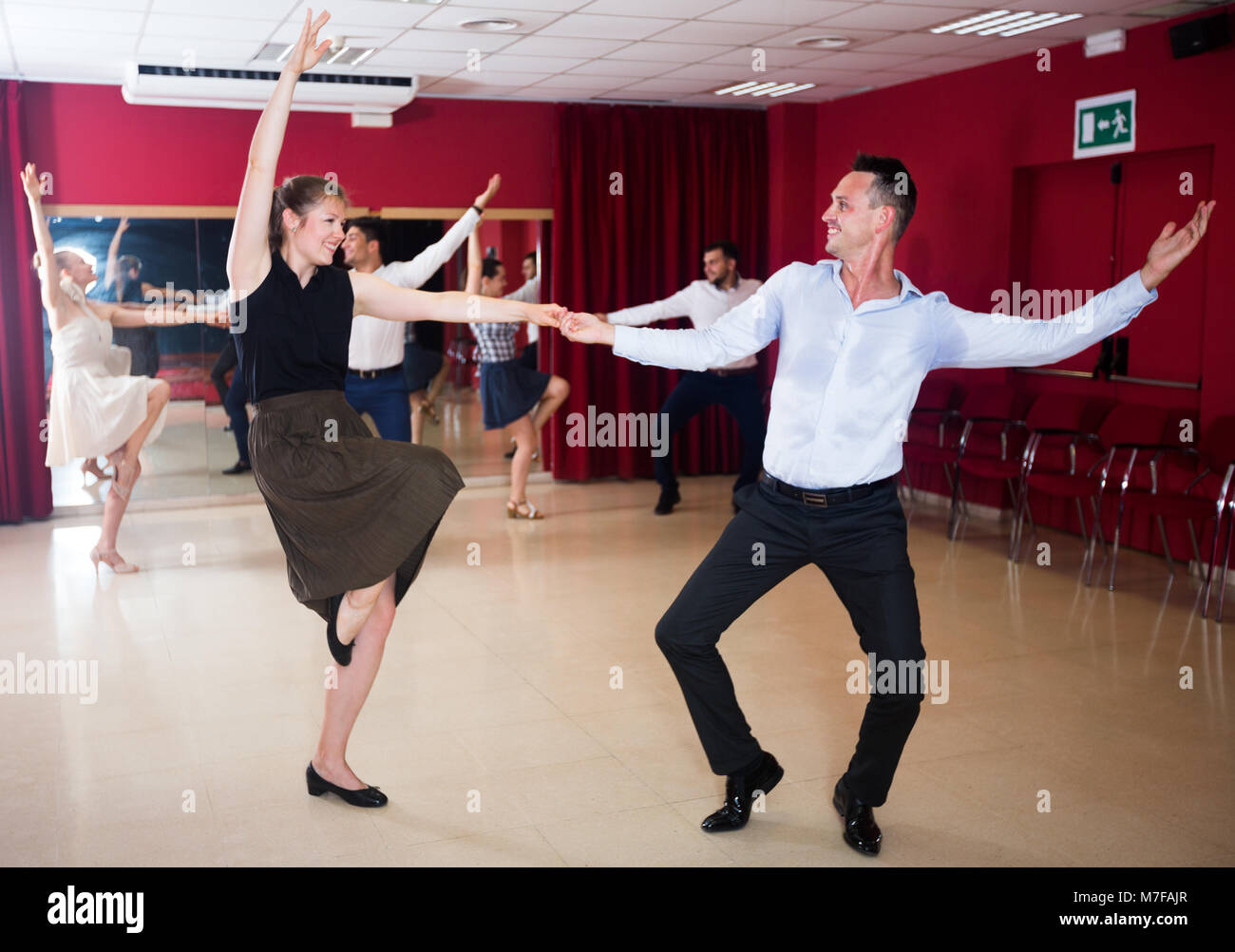Young smiling people practicing vigorous jive movements in dance class ...