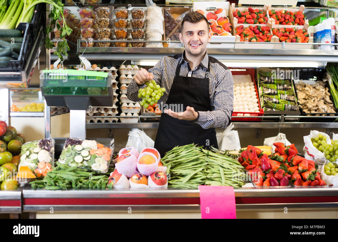 young male seller showing assortment of fruits and vegetables in the ...