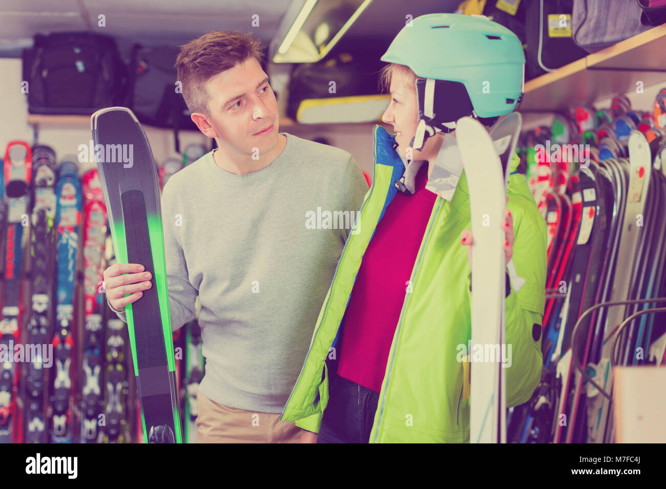 Salesman is helping happy woman in ski equipment to choose ski in sport ...