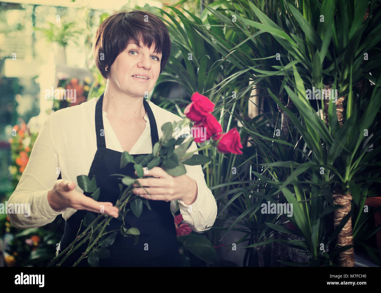 Smiling shop assistant displaying bright red roses in flower shop Stock ...