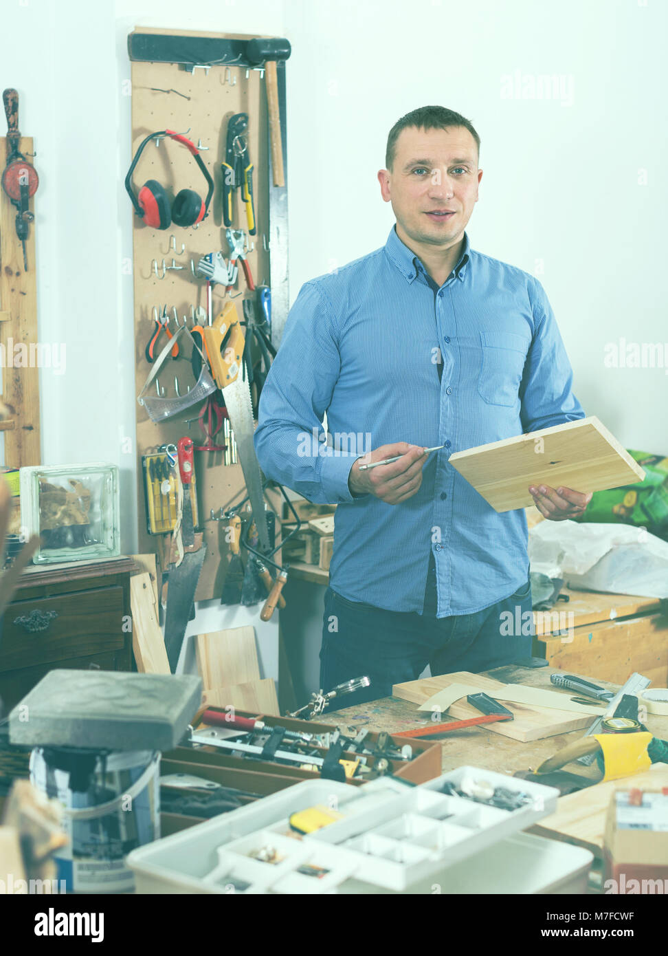 Smiling adult woodworker working with wood plank at workplace Stock ...