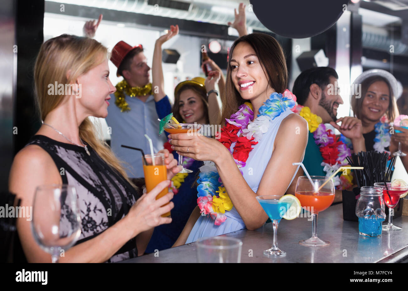Two smiling female in lei are drinking cocktails on hawaiian party ...