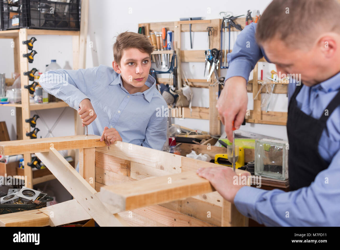 happy germany teacher and boy chiselling a wooden bench in workshop ...
