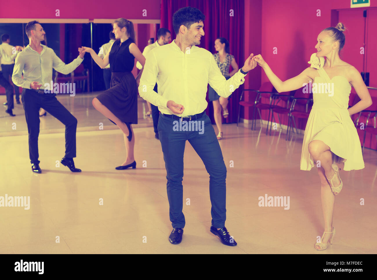 Young smiling people practicing vigorous jive movements in dance class ...