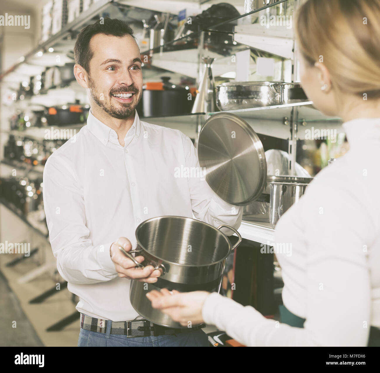 Smiling male seller demonstrating saucepans to customer in dinnerware ...