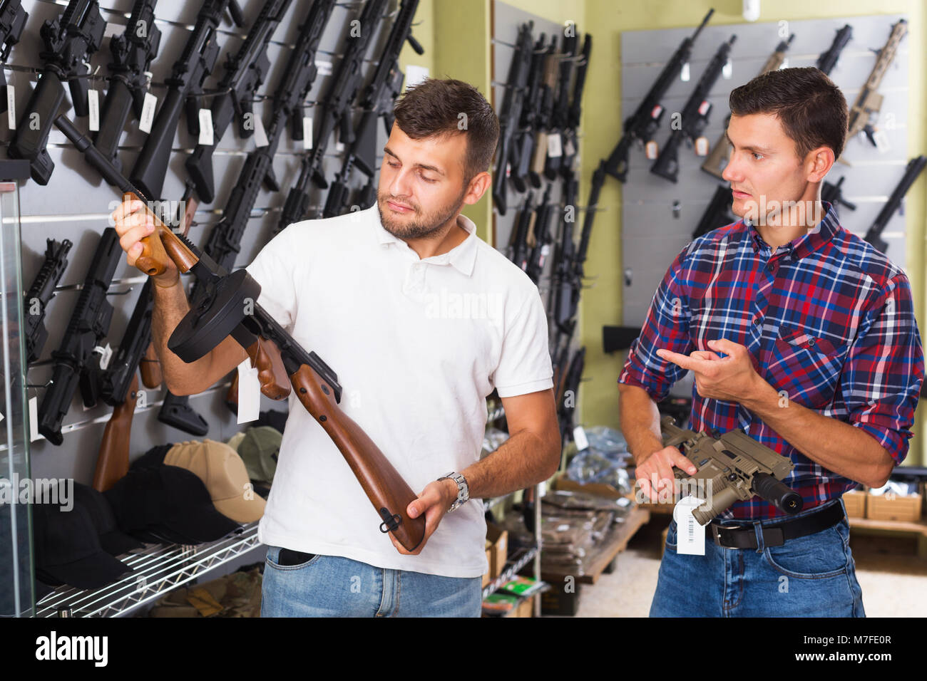 Adult friends choosing air-powered gun in army market Stock Photo - Alamy
