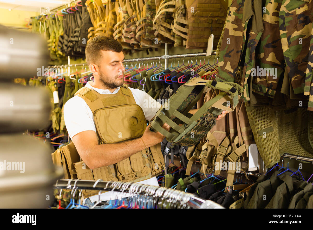 Cheerful adult male customer choose bulletproof vest in army store ...