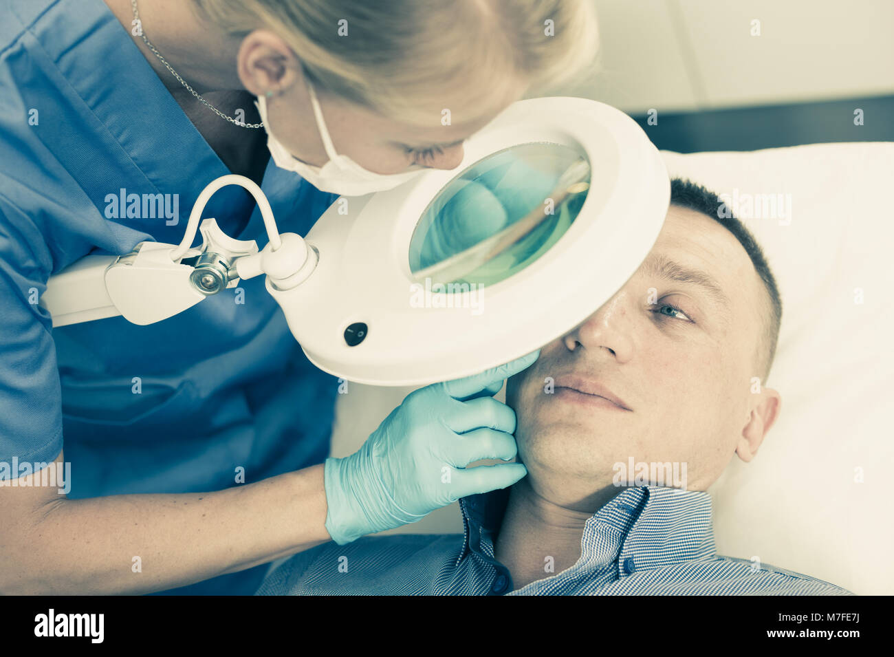 Woman specialist is cleaning skin of patient with using magnification ...