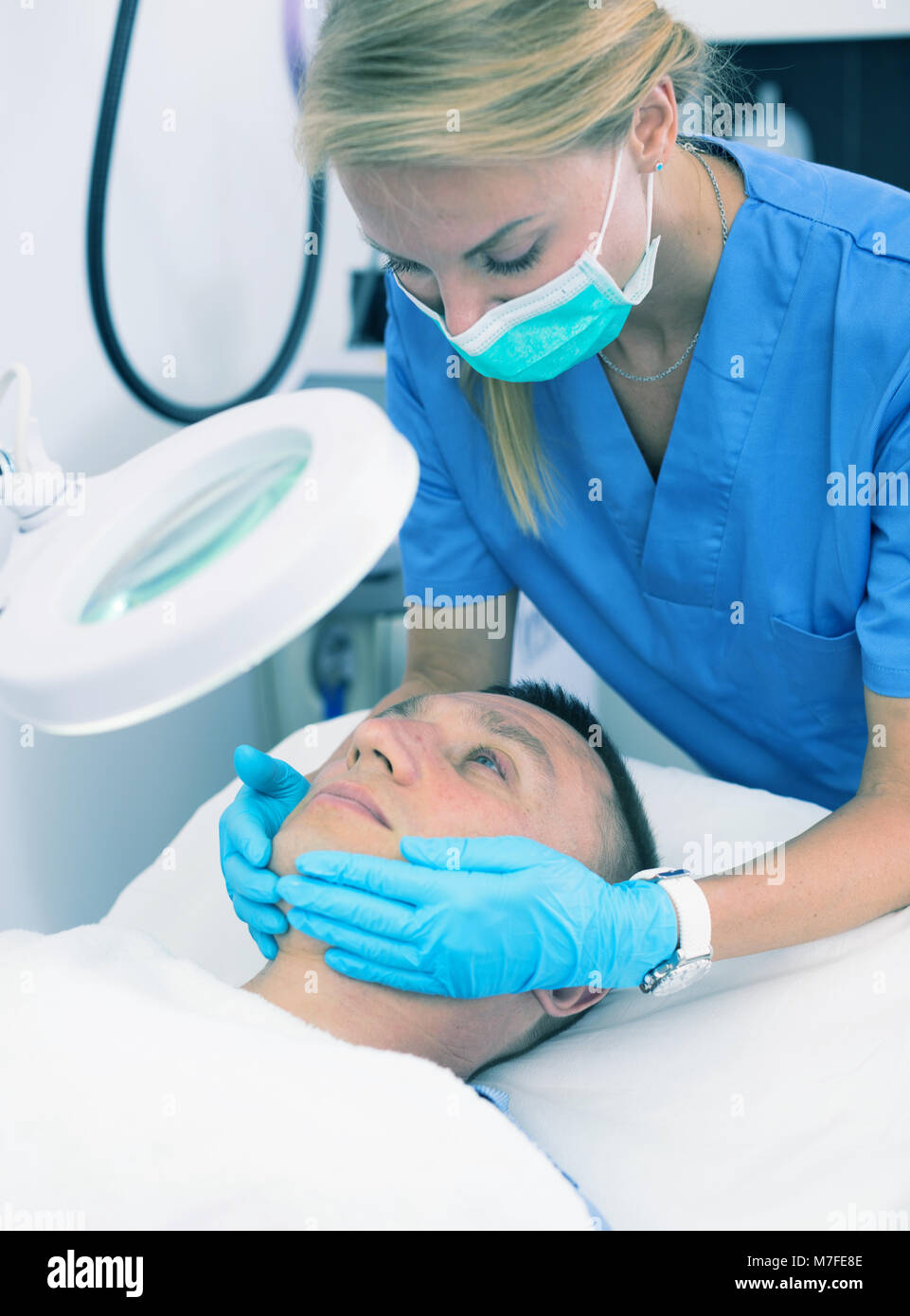 Female doctor is doing massage of skin of face to client in cabinet ...