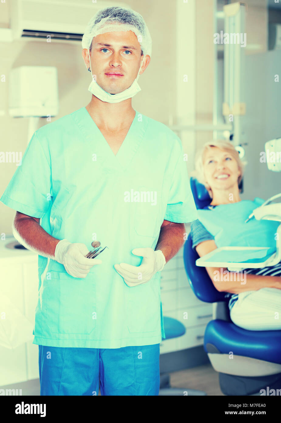 Portrait of professional dentist in dental clinic with patient behind ...