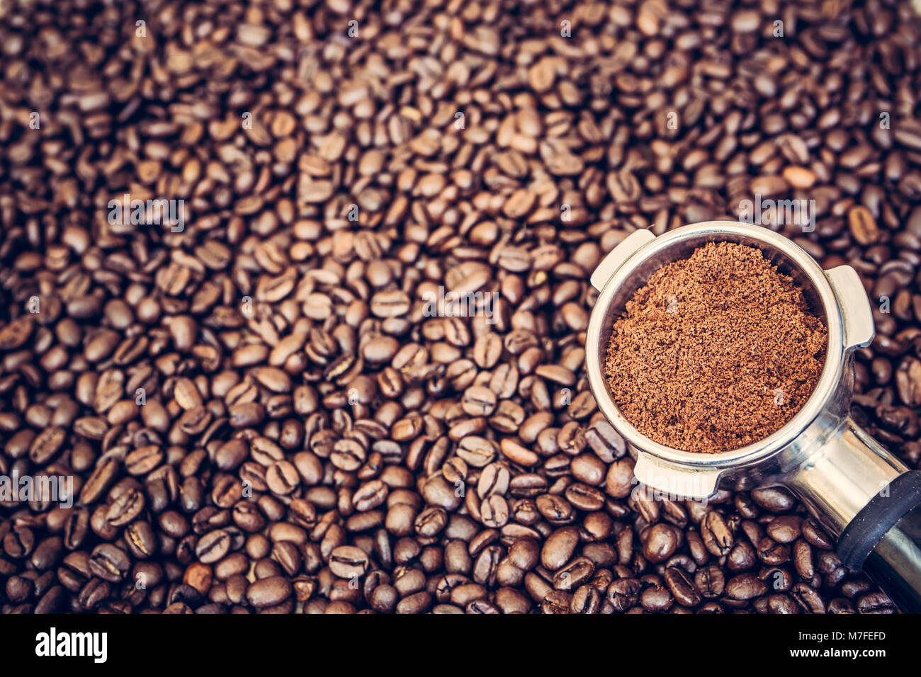 Metal espresso machine scoop with ground coffee on roasted coffee beans ...