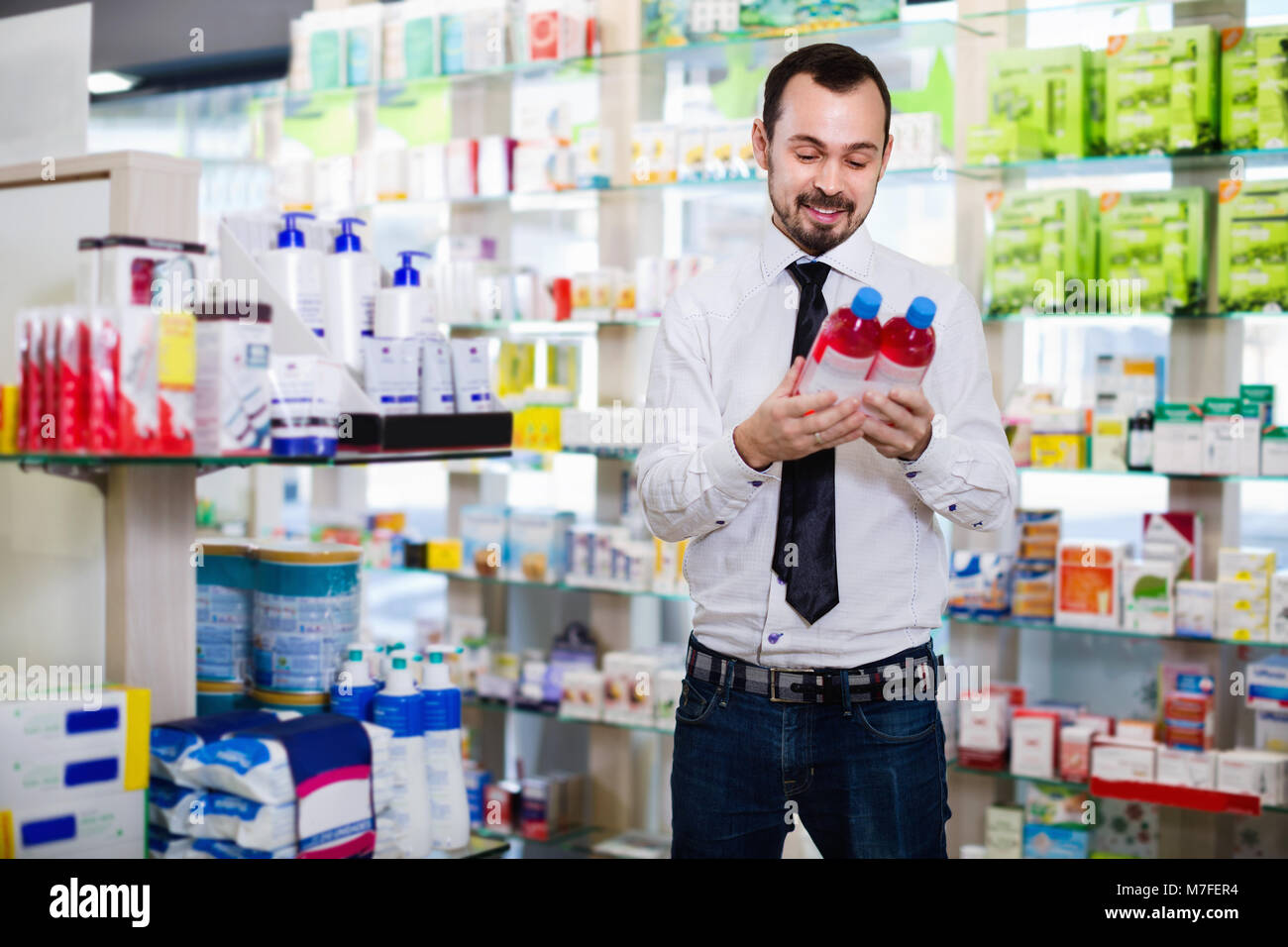 Smiling cheerful male customer looking for right medicine in pharmacy ...