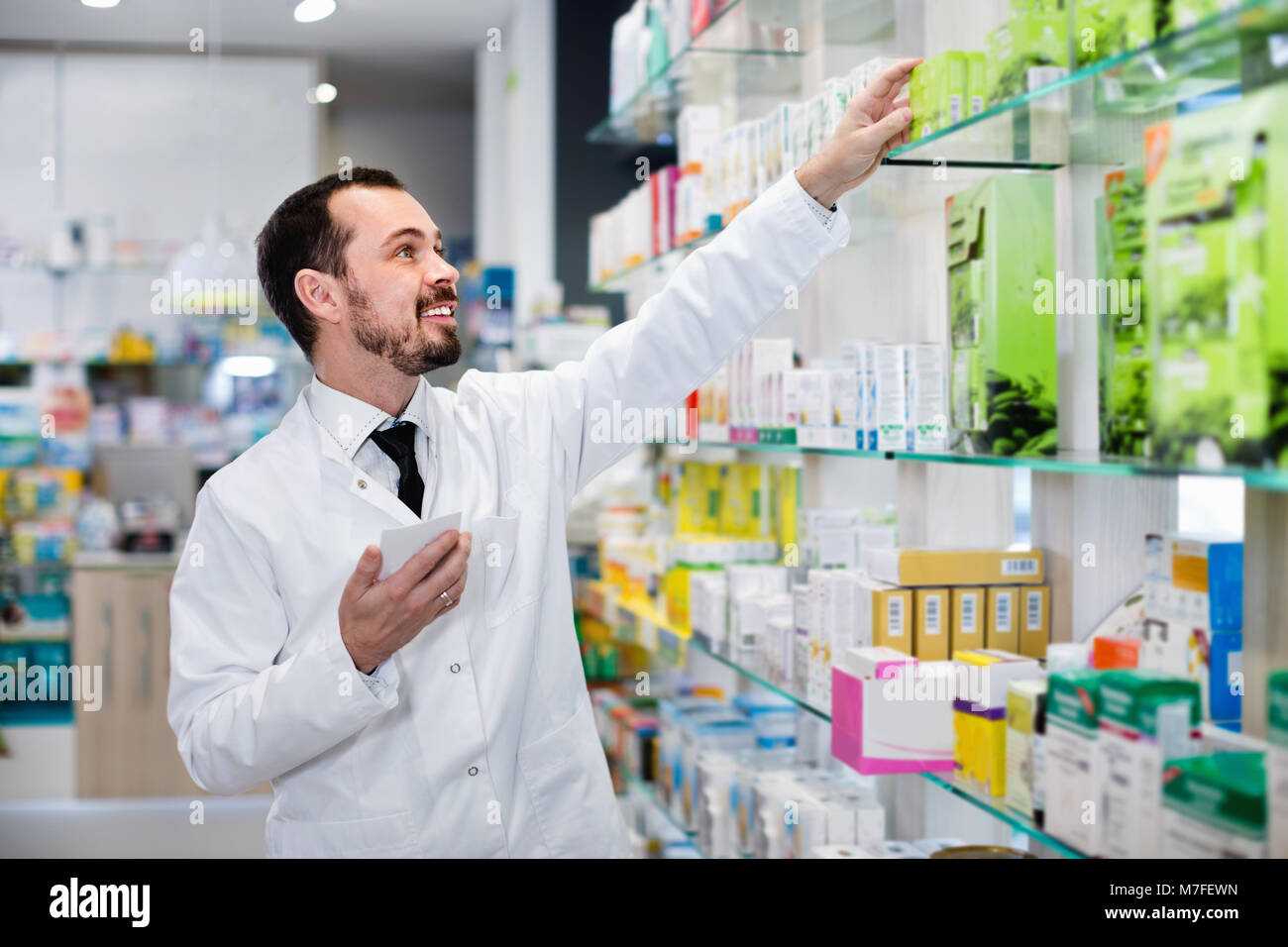 Happy cheerful positive male pharmacist looking for right medicine in ...