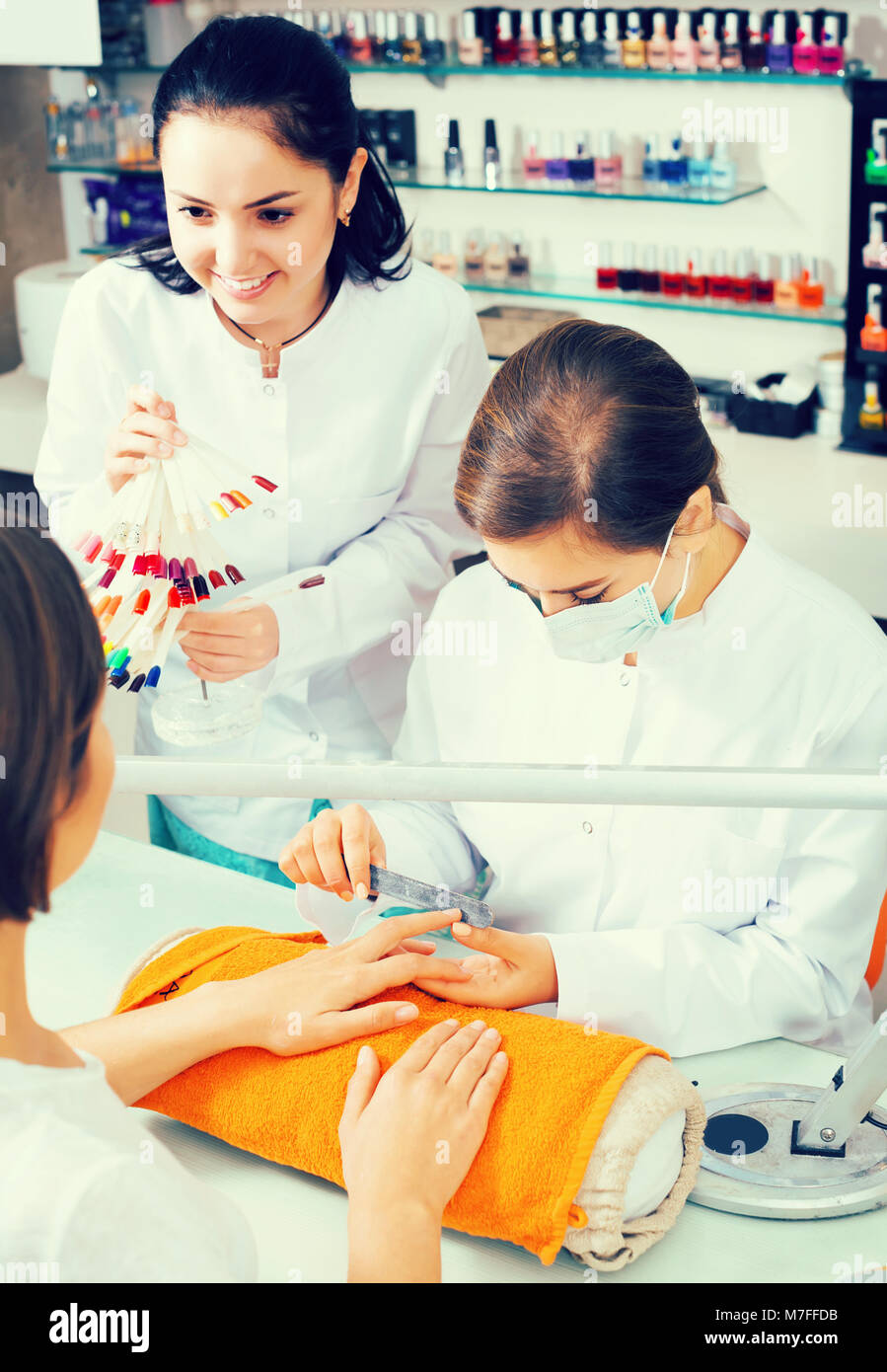 happy manicurists choosing color of nail polish with client in nail ...