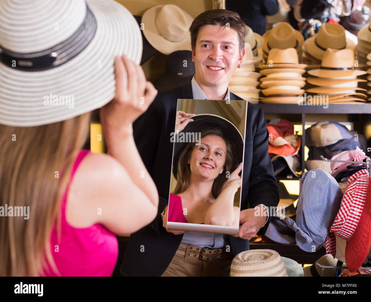 happy man holding mirror and showing customer his reflection in hats ...