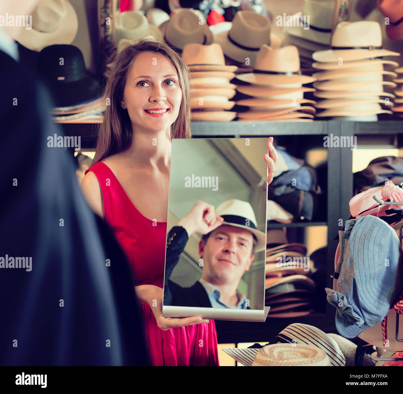 happy european woman holding mirror and showing customer his reflection in hats shop Stock Photo ...