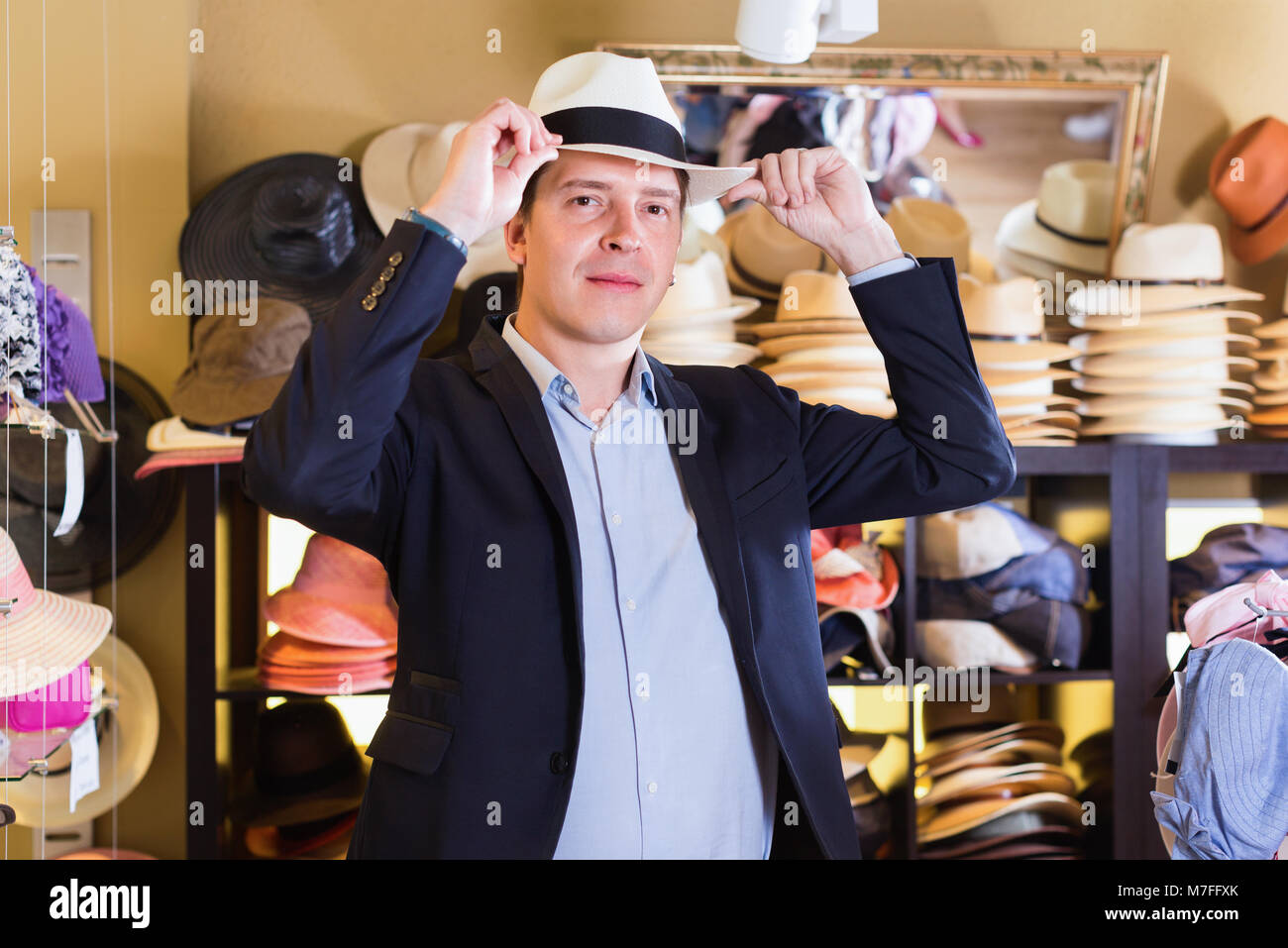 Portrait of cheerful positive young guy try on sun hat at headwear ...