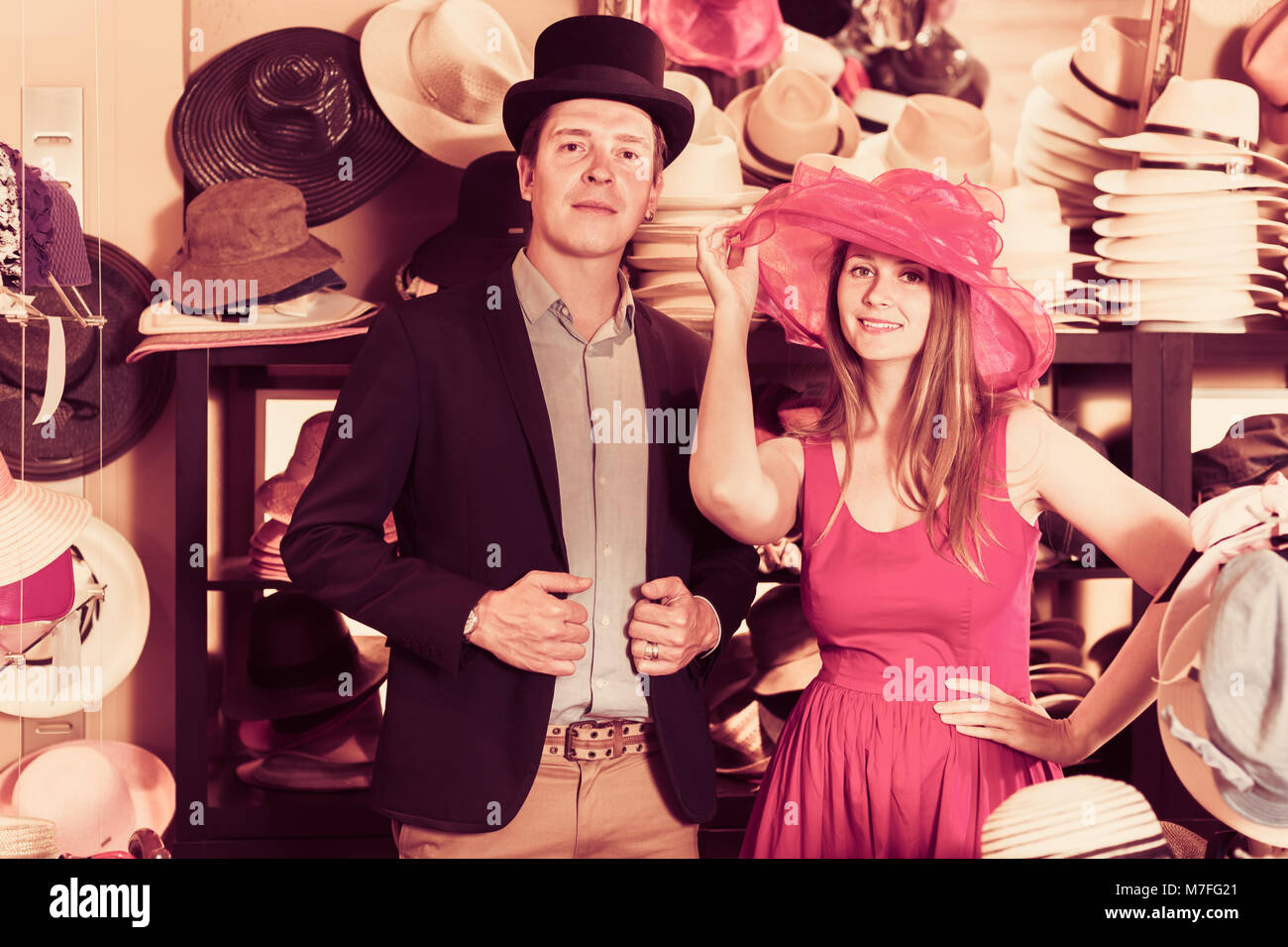 cheerful female and man choosing hats from the assortment in the store ...
